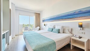 Quarto de hotel com uma cama grande, uma mesa, uma cadeira, um quadro de uma praia e vista para o exterior.