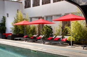 Área de piscina com espreguiçadeiras e guarda-sóis vermelhos.