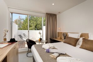 Quarto de hotel com cama, escrivaninha, cadeira, mesinha e varanda com vista para árvores.