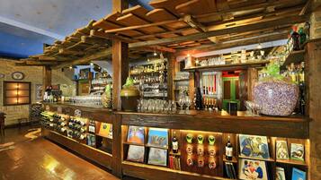 Um bar com vigas de madeira, prateleiras com garrafas, copos e quadros emoldurados.