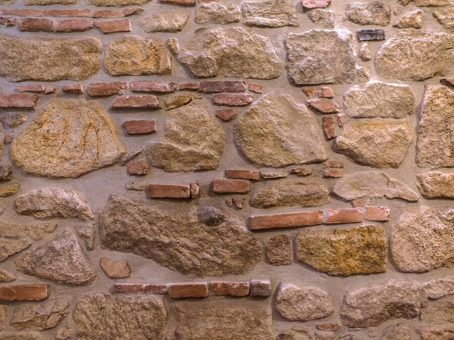 Paredes de pedra com pedras de formatos irregulares e fragmentos de tijolo.