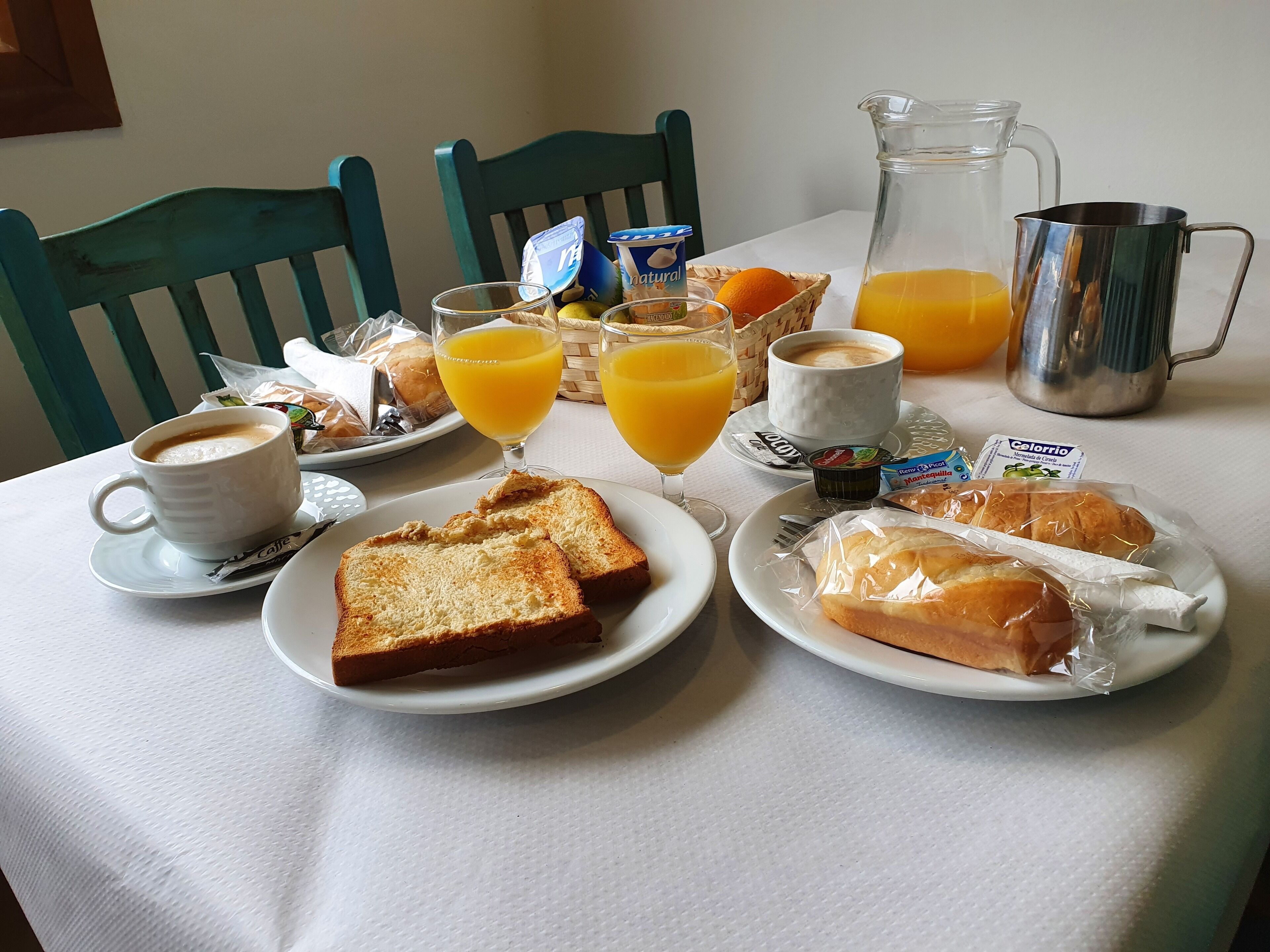 Mesa de café da manhã com torradas, suco de laranja, café e pão.