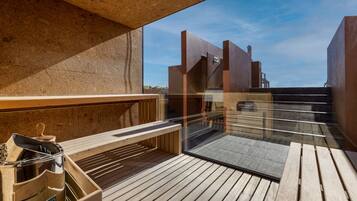 Um deck de madeira com uma sauna, uma porta de vidro que dá para o exterior e vista para um edifício moderno.