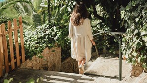 Uma pessoa caminhando por uma escadaria de pedra, cercada por vegetação exuberante e uma piscina ao fundo.