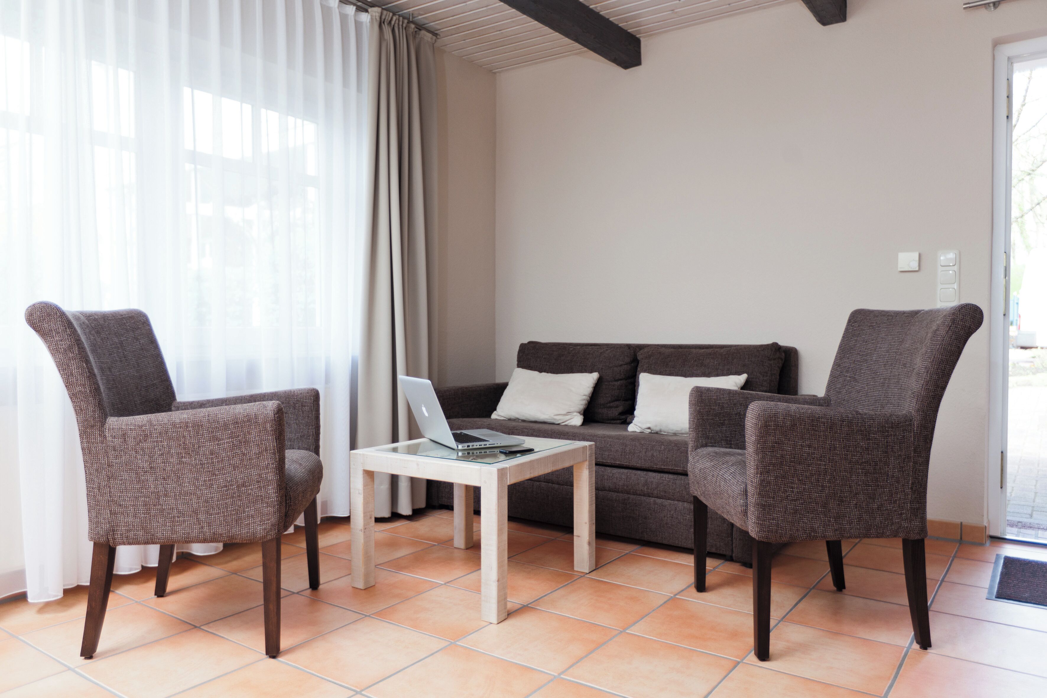 Uma sala de estar com sofá, duas poltronas, mesa de centro e um laptop.