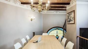 Uma sala de conferências com mesa de madeira, cadeiras brancas, um candelabro e uma janela de vitrais.
