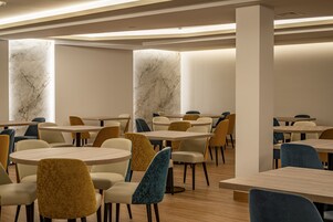 Uma área de refeições moderna com mesas e cadeiras redondas, paredes de mármore e iluminação embutida.