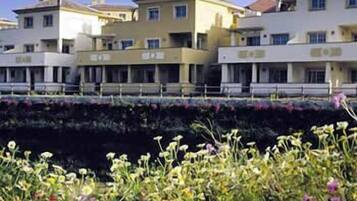 Uma fileira de edifícios residenciais modernos, com dois andares e varandas, localizada perto de um corpo d'água, com flores em plena floração ao primeiro plano.