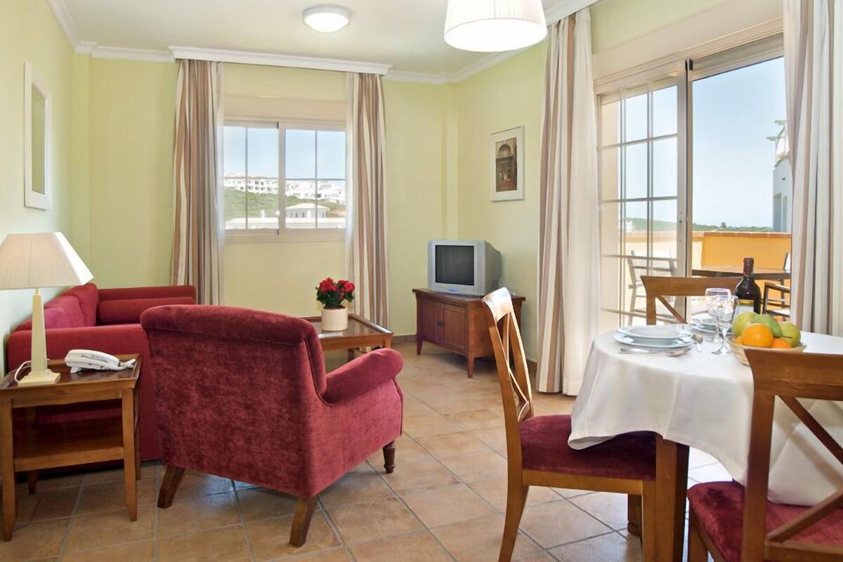 Quarto de hotel com área de refeições, televisão, sofá e vista para o mar.