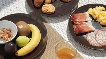 Uma mesa com pratos de comida, um copo de suco e talheres sobre uma toalha de tecido trançado.