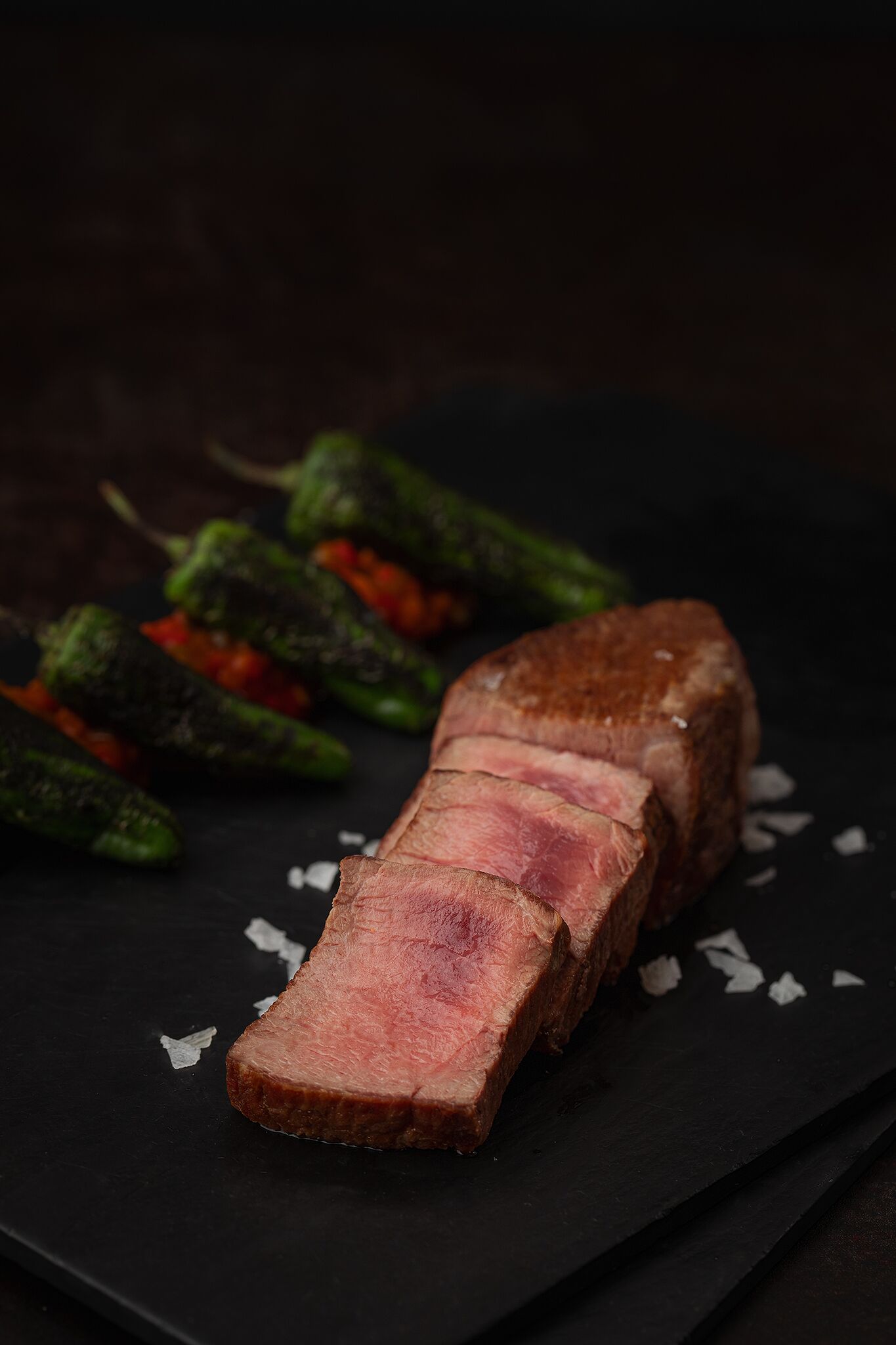 Bife ao ponto para mal servido em prato preto, com sal e legumes grelhados.