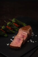 Bife ao ponto para mal servido em prato preto, com sal e legumes grelhados.