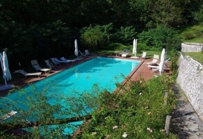 Uma piscina retangular com água azul cristalina, rodeada por espreguiçadeiras e guarda-sóis.