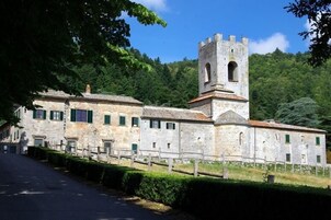 Um edifício histórico de pedra com uma torre, apresentando uma série de janelas e um caminho pavimentado que o leva até ele.