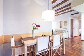 Uma área de refeições com uma mesa de madeira, cadeiras brancas, um vaso com flores e um candeeiro pendente.