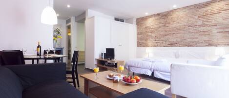 Quarto de hotel moderno com área de refeições, televisão, cama e preparação para café da manhã.