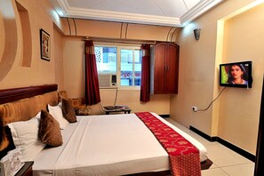 Quarto de hotel com uma cama, televisão, janela com cortinas e ar condicionado fixado na parede.
