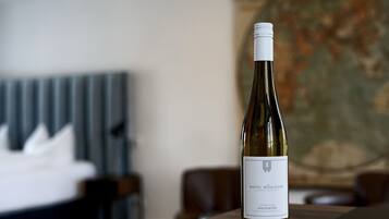 Uma garrafa de vinho do Hotel Mühlendorf sobre uma mesa, com um fundo desfocado de uma cama e um quadro.