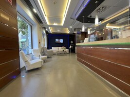 Uma área de recepção moderna, com um balcão de madeira, assentos confortáveis e uma tela de televisão.