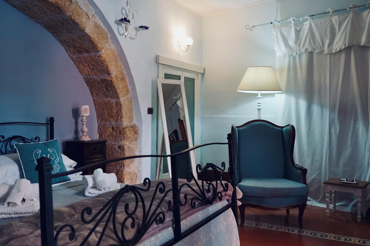 Quarto com cama, uma cadeira, mesa de cabeceira, abajur e cortina.