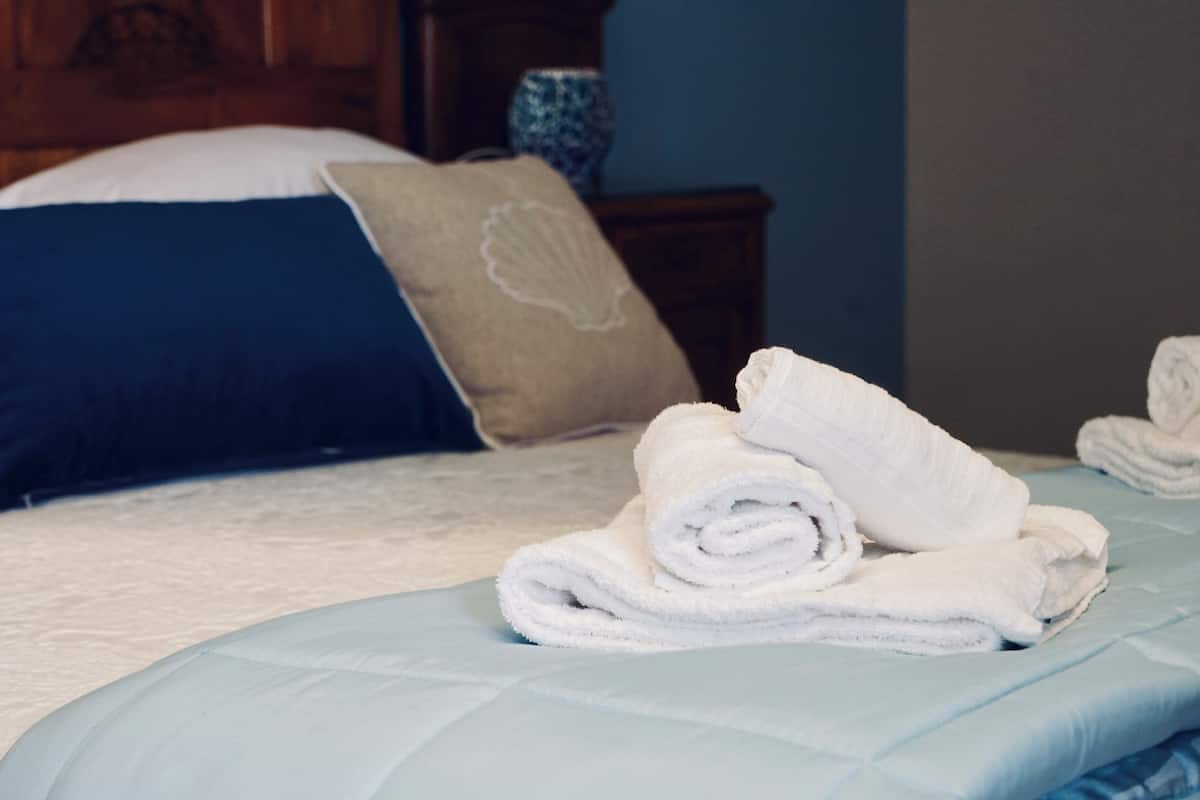 Cama bem arrumada com almofadas azuis e bege, colcha azul e toalhas brancas dobradas sobre a cama.
