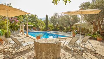 Área de piscina com espreguiçadeiras e guarda-sóis, cercada por árvores e plantas em vasos.