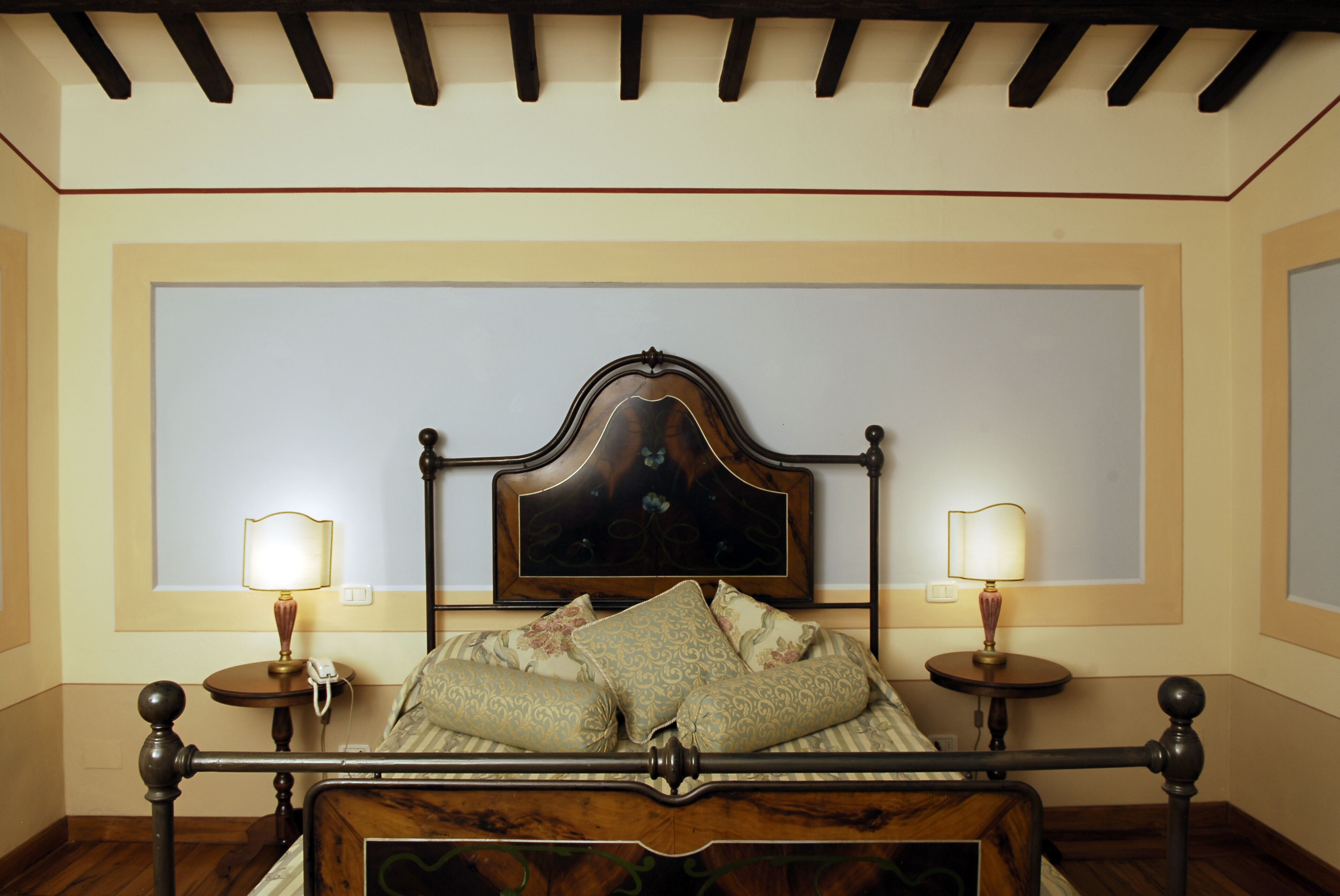 Uma cama bem arrumada com cabeceira de madeira, duas mesas de cabeceira com abajures e um espelho sobre a cama.