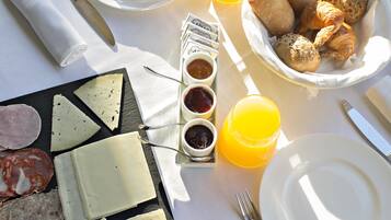 Uma mesa de café da manhã com diversos alimentos, como torradas, queijo, pão, croissants e um prato de frutas.