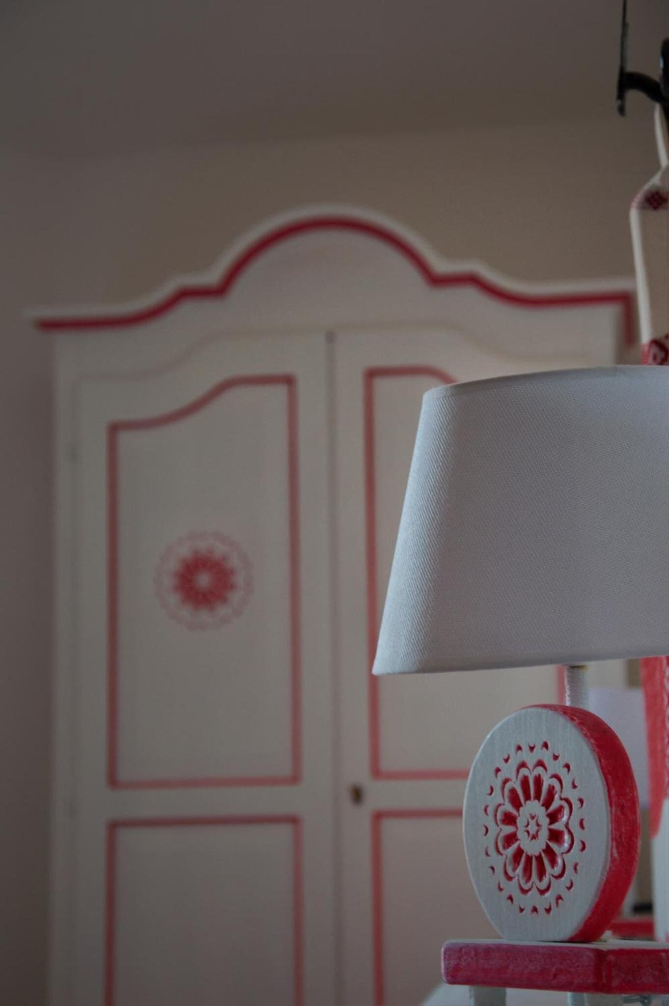 Quarto com cabeceira estampada em branco e vermelho e abajur com base vermelha.