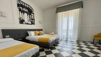 Quarto de hotel com duas camas, piso xadrez, uma janela grande com cortinas e uma cadeira amarela.