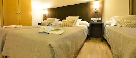 Quarto de hotel com duas camas, um guarda-roupa de madeira e uma mesa de cabeceira com abajur.