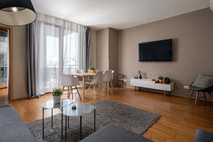 Uma sala de estar moderna com área de jantar, uma TV de tela plana na parede e uma grande janela com cortinas leves.