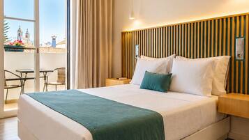 Quarto de hotel moderno com uma cama grande, piso de madeira, vista para a cidade e varanda com área de estar ao ar livre.