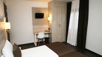 Quarto de hotel com uma cama, uma escrivaninha, uma cadeira, uma TV e cortinas.