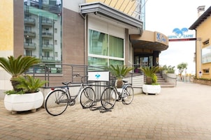 Entrada de hotel com suporte para bicicletas, vasos de plantas e placa indicando Hotel Capri.