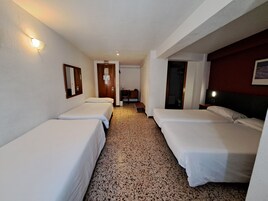 Quarto de hotel com duas camas de solteiro, uma porta de madeira, uma pequena mesa e um espelho na parede.