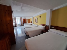 Quarto de hotel com quatro camas, um guarda-roupa de madeira, uma mesinha e um espelho.