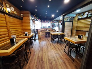 Interior de restaurante com paredes, mesas e cadeiras de madeira.