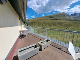 Uma varanda com mesa e cadeiras, corrimão e vista para uma paisagem montanhosa.