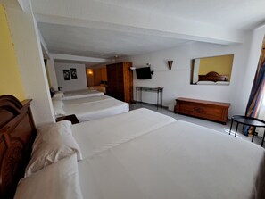 Quarto de hotel com três camas, uma cômoda de madeira, uma TV e um espelho.