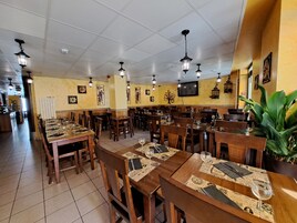 Um restaurante com várias mesas e cadeiras de madeira, piso de azulejos e luminárias pendentes em estilo lanterna.