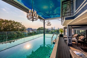 Piscina infinita no terraço com barreira de vidro, cadeiras de lounge e vista para a cidade.