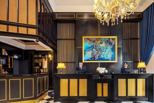 Uma área de recepção com esquema de cores preto e dourado, uma pintura grande e um candelabro.