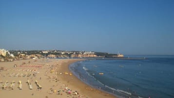 Uma praia com fileiras de guarda-sóis e espreguiçadeiras, céu claro e mar calmo.