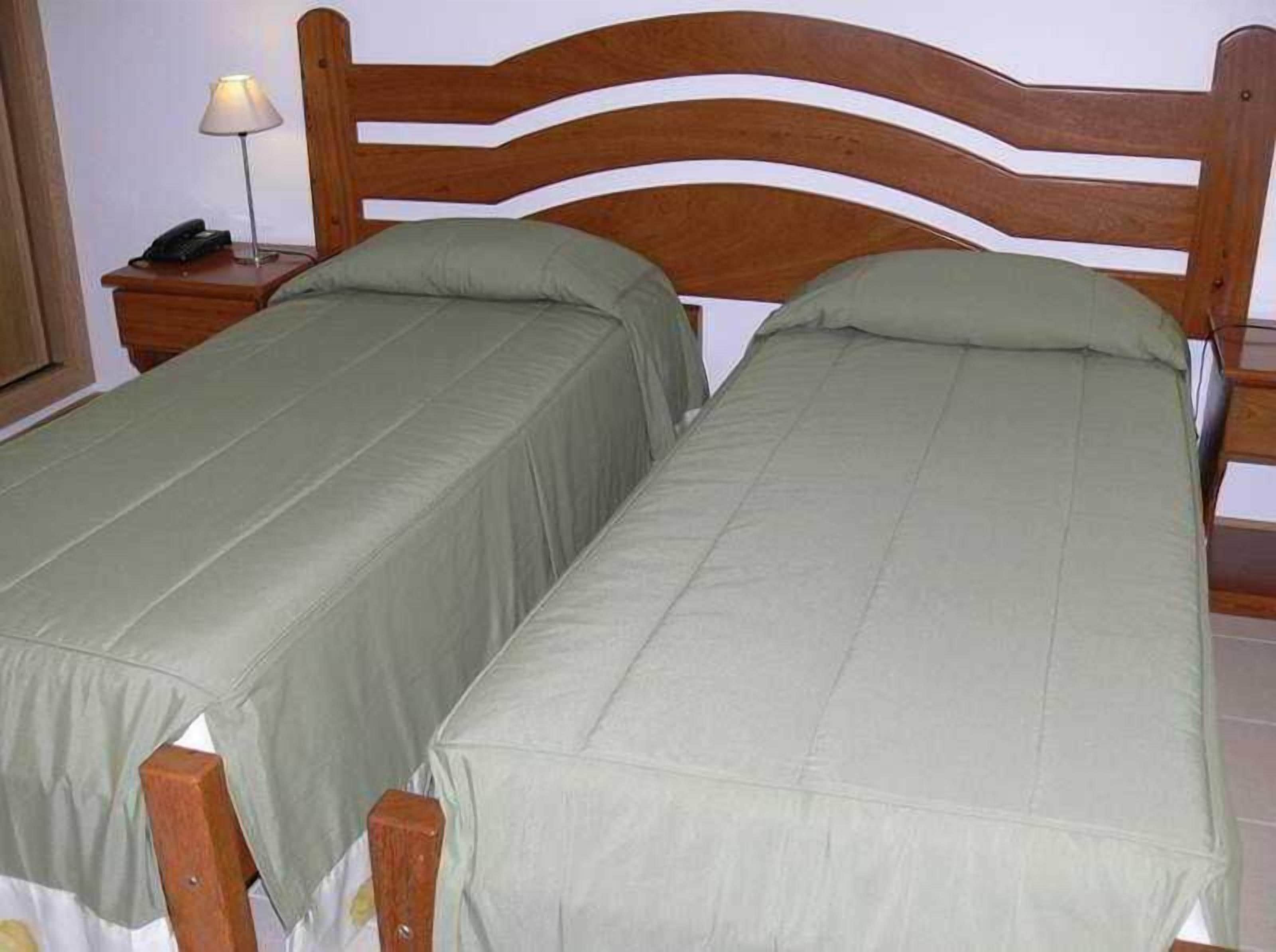 Quarto com duas camas de solteiro, cabeceiras de madeira, mesa de cabeceira com abajur e telefone.