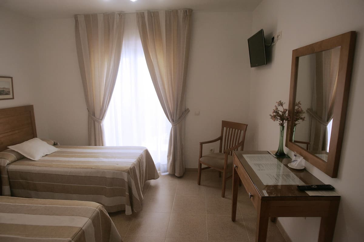 Quarto de hotel com duas camas, uma escrivaninha, uma cadeira, uma televisão e um espelho.