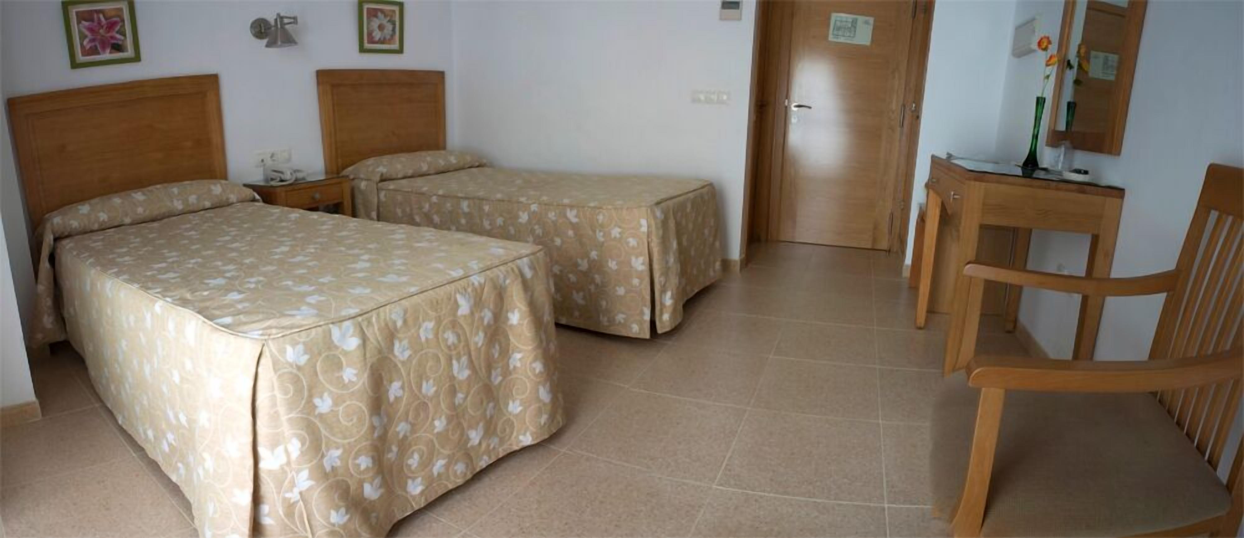 Quarto de hotel com duas camas, uma escrivaninha e uma cadeira.