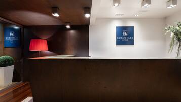 Balcão de recepção com luminária vermelha, duas placas para Eurostars Hotels e uma pequena planta.