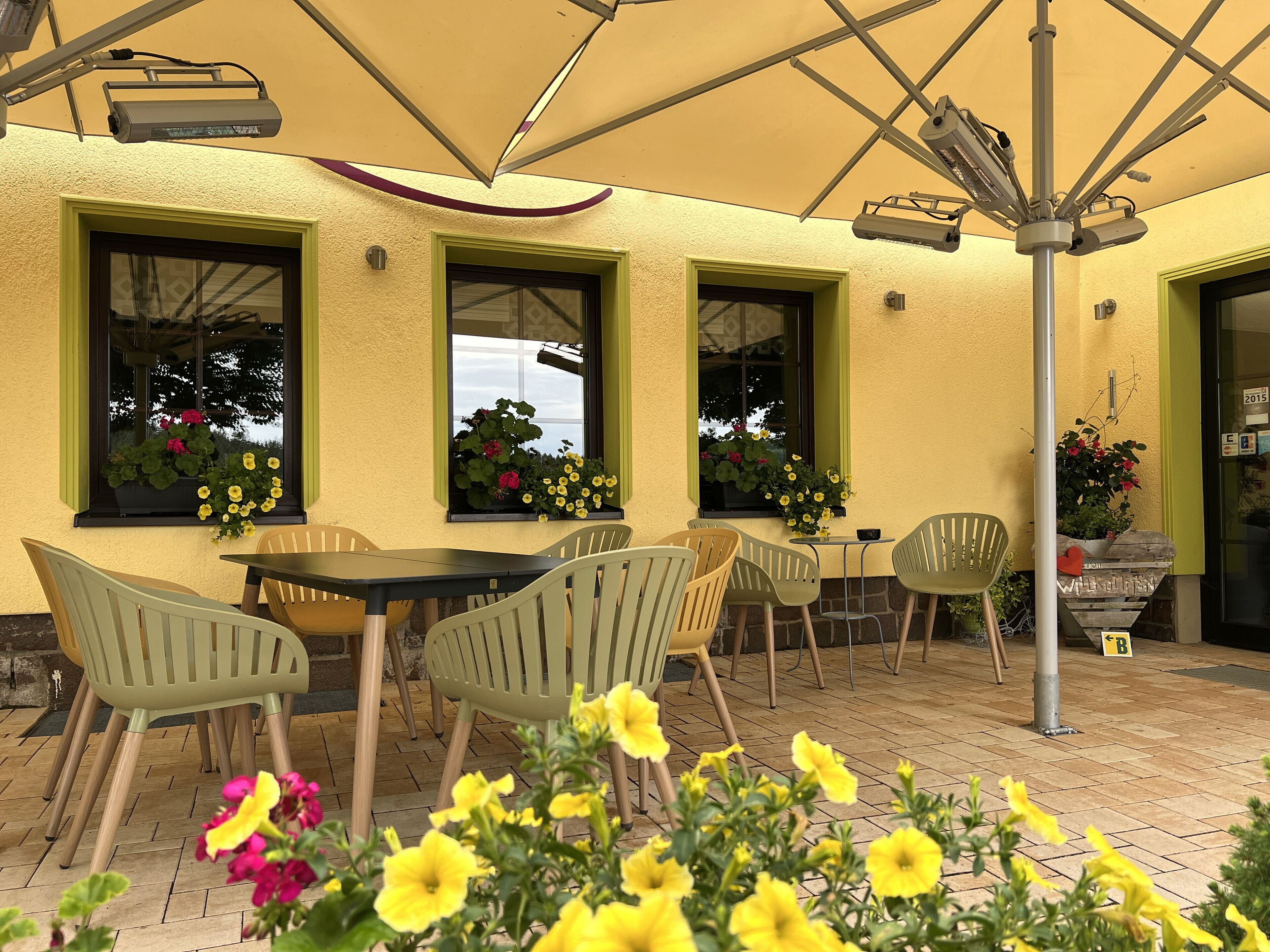 Um pátio externo com mesa e cadeiras, uma parede amarela e jardineiras nas janelas.