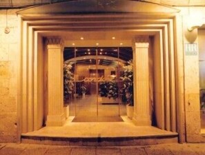 Entrada de hotel com um arco imponente, balcão de recepção e uma placa com a inscrição 'Hotel'.